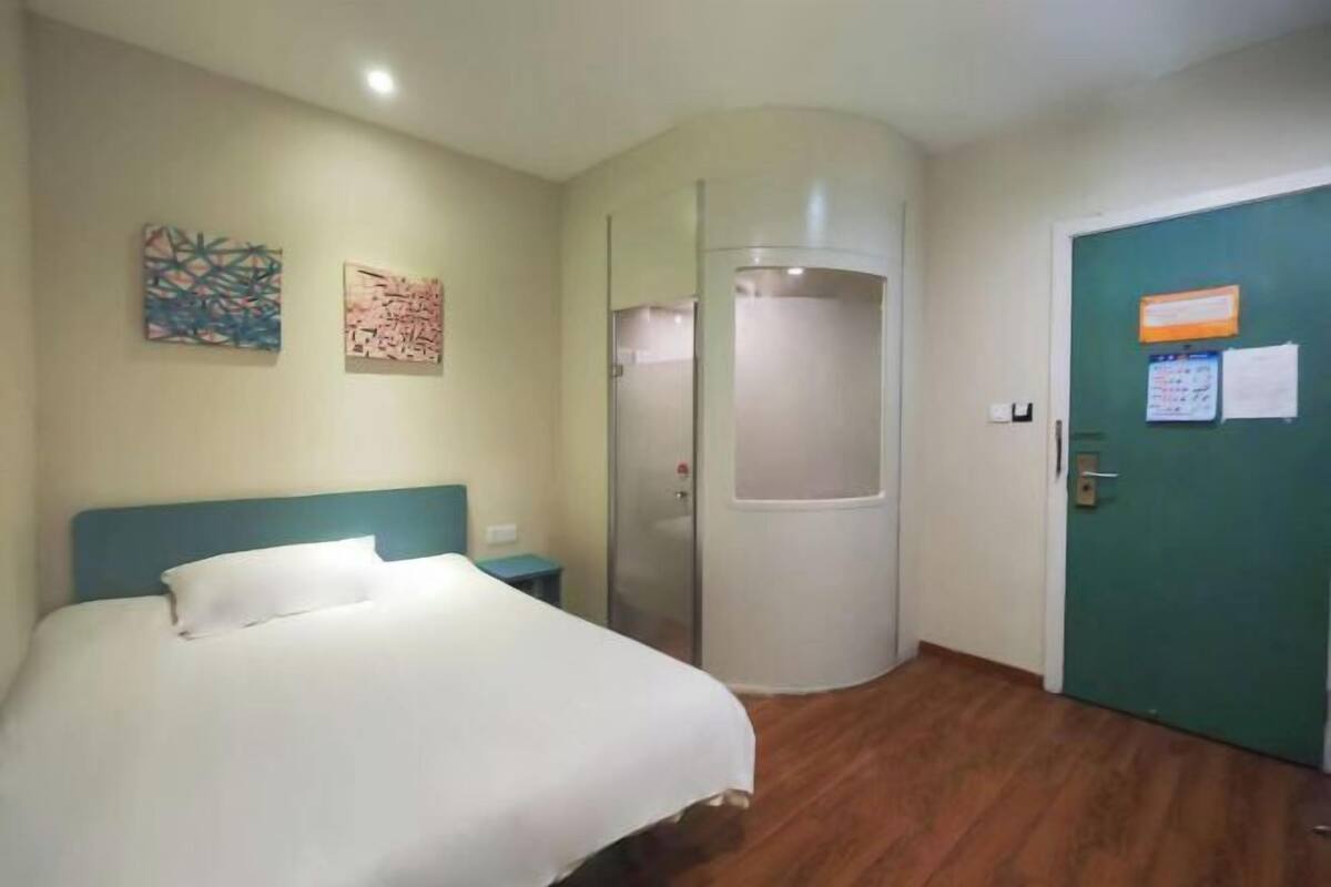 Quarto de hotel com uma cama, chuveiro e porta com painel verde.