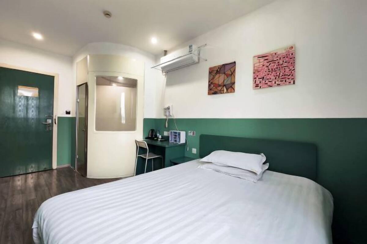Quarto de hotel com cama, escrivaninha, cadeira e duas pinturas abstratas na parede.