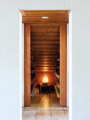 Um corredor de madeira com luminária central, ladeado por prateleiras com garrafas.