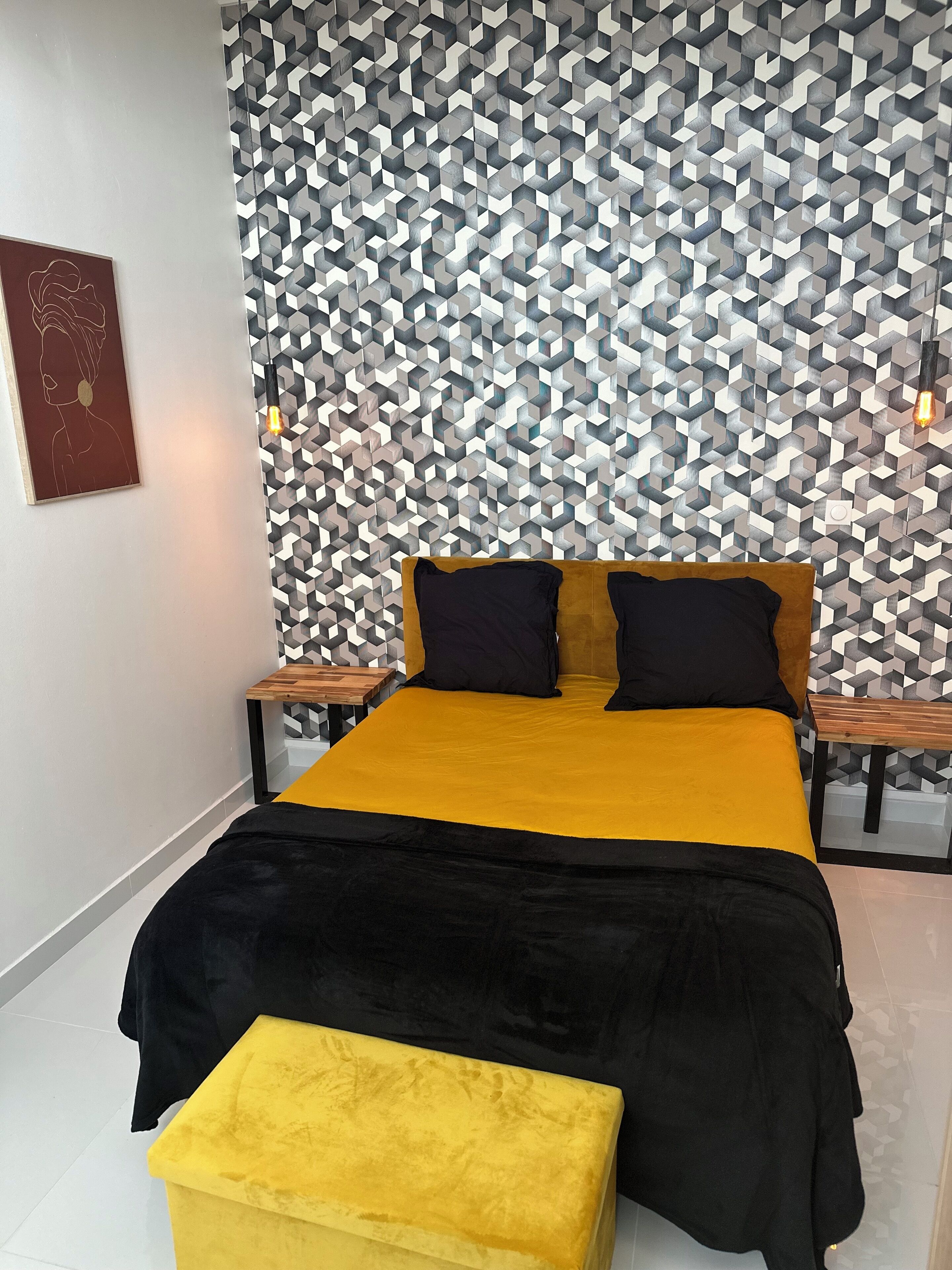 Quarto moderno com papel de parede estampado com padrão geométrico, colcha amarela, almofadas pretas e amarelas e um banquinho amarelo.