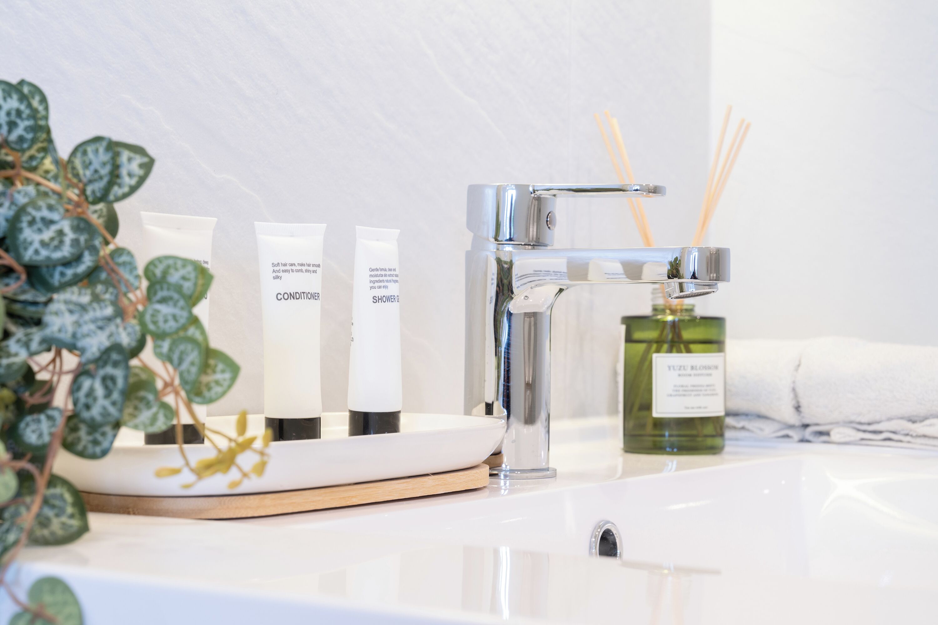 Um banheiro com pia branca, frasco verde de hidratante corporal Yuzu Blossom, toalha branca e dois tubos de condicionador e gel de banho.