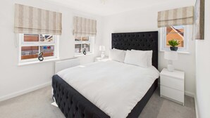 Quarto com cama grande, paredes brancas, cabeceira preta e duas mesas de cabeceira com abajures.