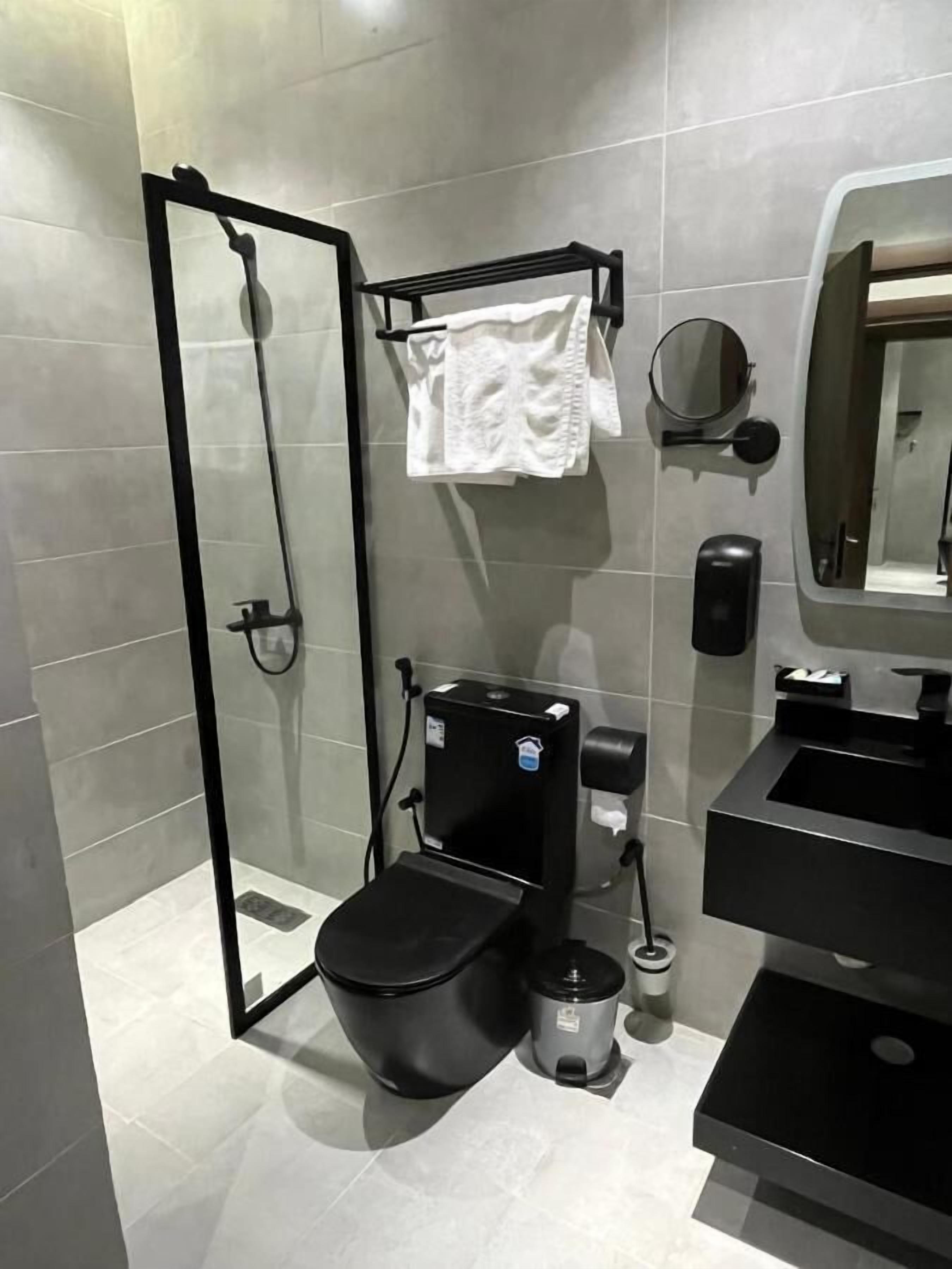 Uma casa de banho moderna com chuveiro envidraçado, sanita preta, lavatório e espelho.