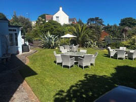 Jardim bem cuidado com área de refeições, móveis de vime e um guarda-sol branco.