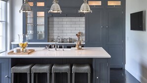 Uma cozinha moderna com armários azul escuro, uma ilha branca e três luminárias pendentes.