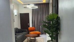Uma sala de estar moderna com um sofá cinzento, uma poltrona laranja, uma mesa de centro redonda de madeira e uma grande planta em vaso.