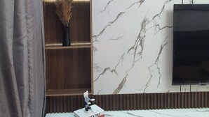 Sala de estar moderna com parede estampada em mármore, televisão montada e estantes de madeira com objetos decorativos.