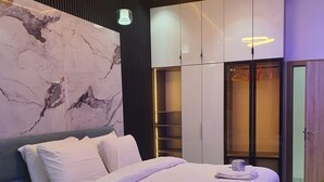 Quarto moderno com cama grande, roupeiro embutido e parede de destaque em mármore.