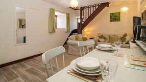Uma sala de jantar com uma mesa posta para quatro pessoas, uma escada e um sofá ao fundo.