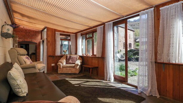 Um quarto aconchegante com teto de madeira, um sofá marrom, uma cadeira e uma janela grande com cortinas.