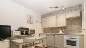 Uma cozinha moderna com armários brancos, forno embutido, micro-ondas, máquina de café e um espaço de refeições com duas cadeiras.