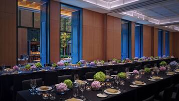 Uma longa mesa de jantar posta para um evento formal, com diversas cadeiras, velas e arranjos florais.