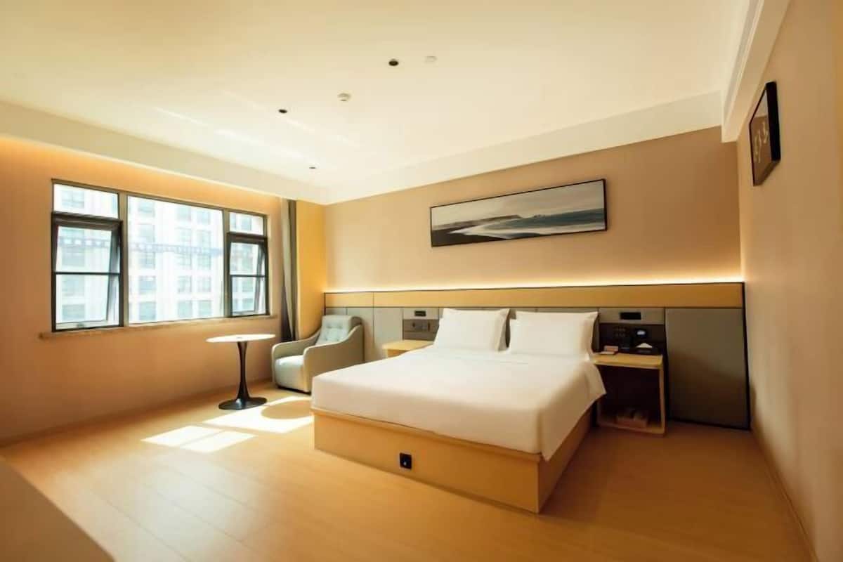 Quarto de hotel moderno com uma cama grande, mesas de cabeceira, uma cadeira e uma janela com vista.