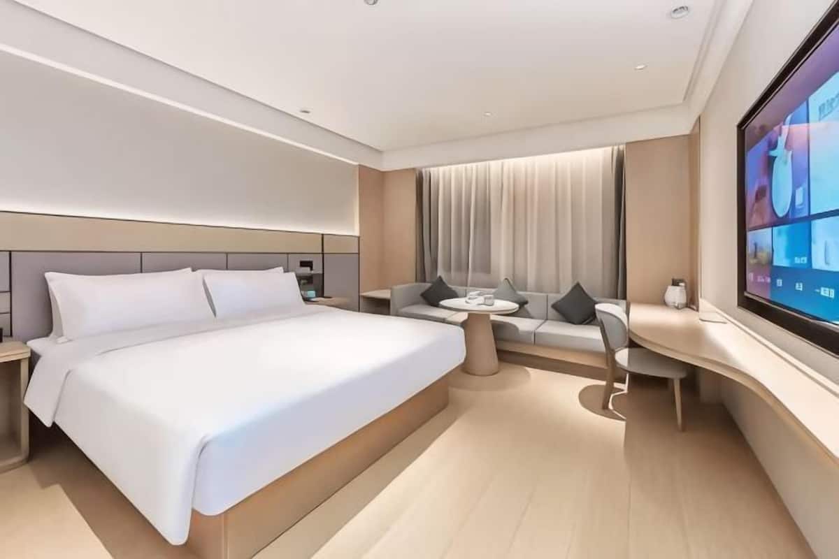 Quarto de hotel moderno com uma cama grande, um sofá, uma mesa pequena e uma tela de televisão.