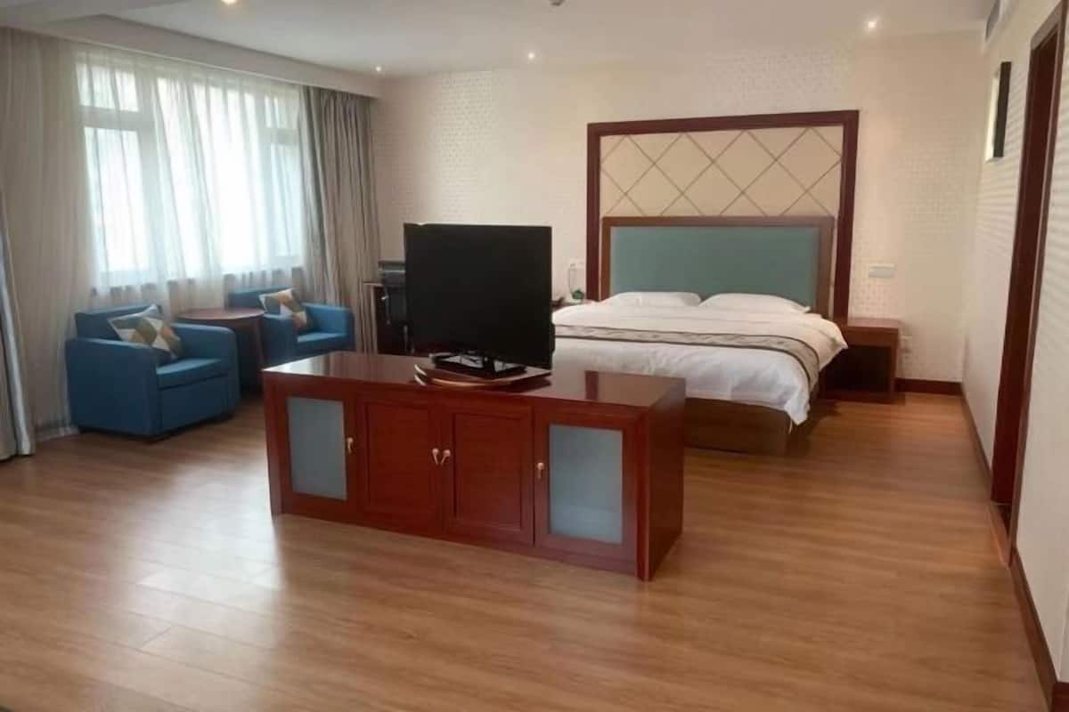 Quarto de hotel com cama, televisão, escrivaninha e área de estar com cadeiras.