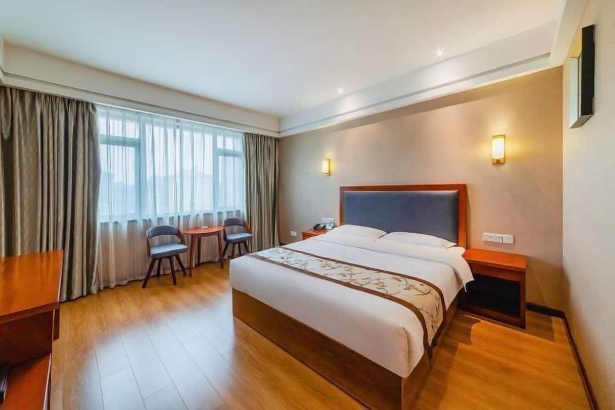 Quarto de hotel com uma cama grande, uma escrivaninha, duas cadeiras e uma janela com cortinas.