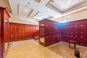 Quarto de hotel com um espelho grande, um banco vermelho e piso estampado.