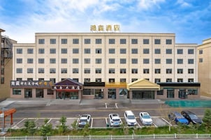 Hotel com vários andares, entrada central, estacionamento e diversos estabelecimentos comerciais no térreo.