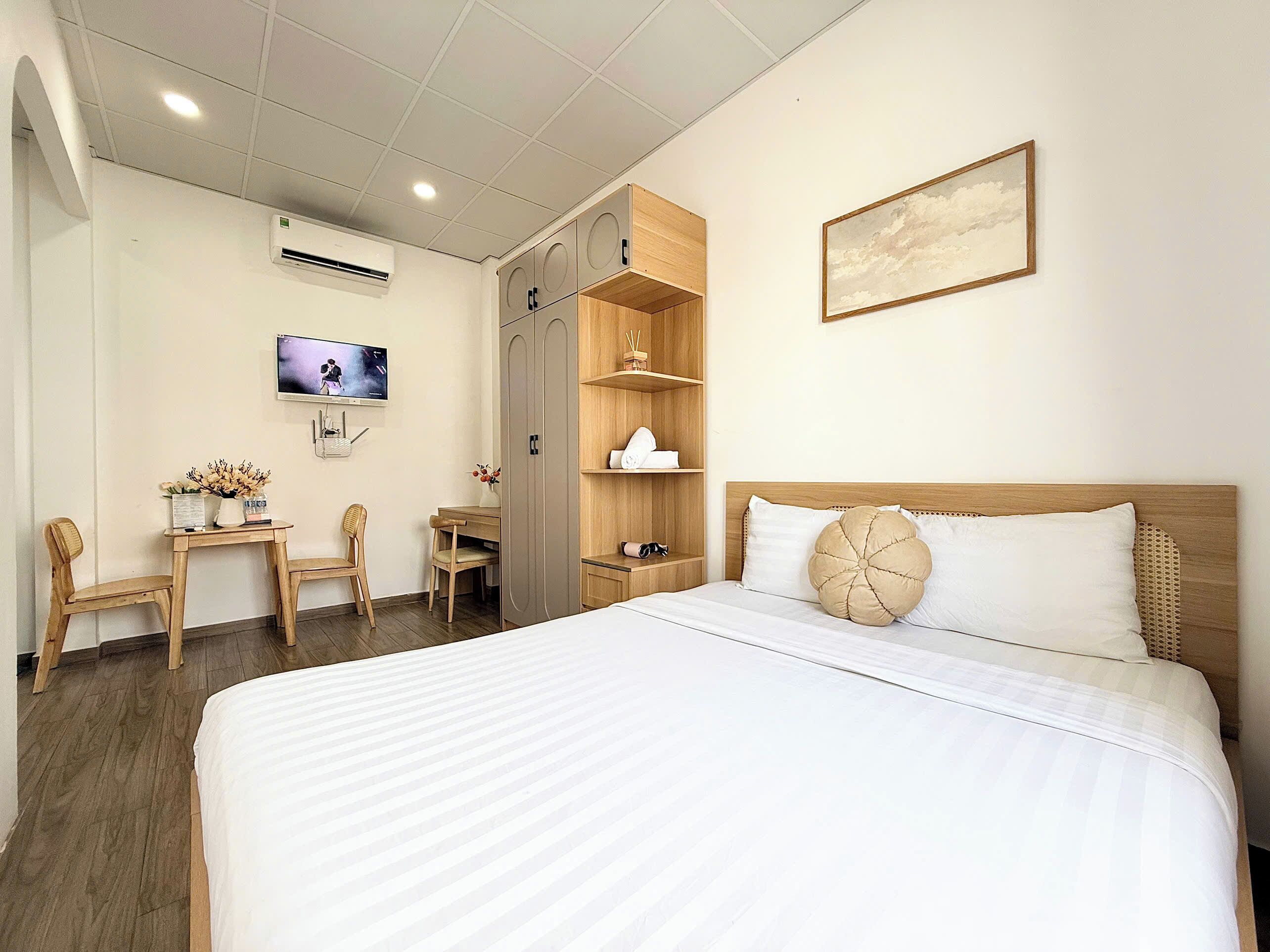 Quarto de hotel com cama, escrivaninha, cadeiras, televisão, guarda-roupa e um quadro na parede.