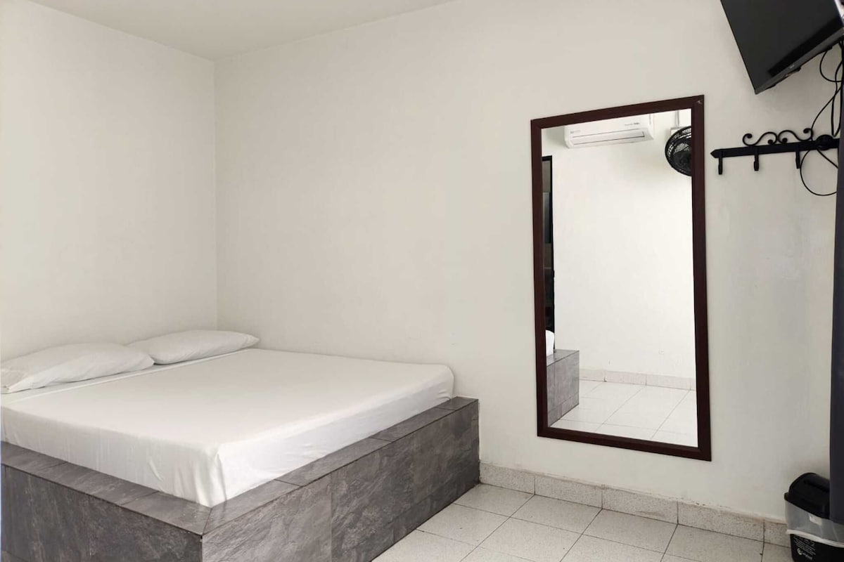 Quarto com cama, um espelho grande, televisão e aquecedor fixado na parede.
