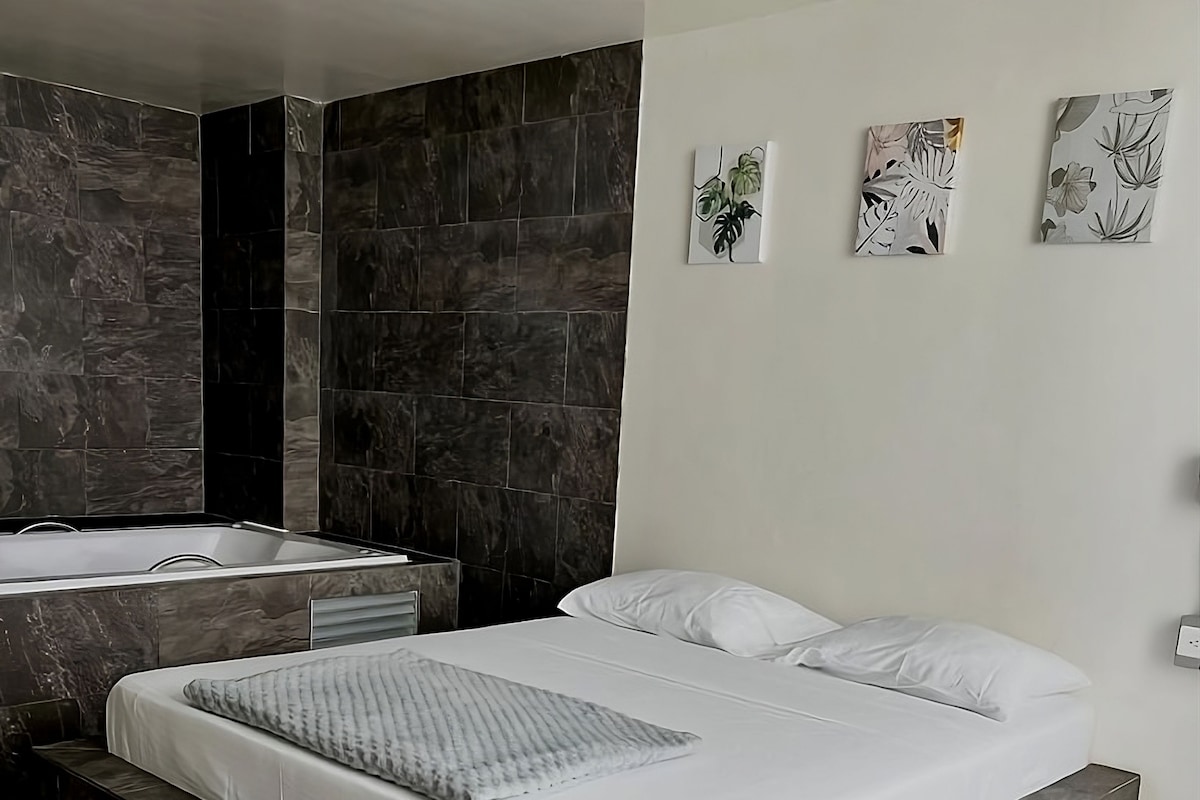 Quarto moderno com uma cama grande, um banco embutido, banheiro separado com banheira e três obras de arte na parede.