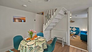 Uma sala de jantar com uma mesa posta para quatro pessoas, uma escadaria e uma sala de estar com um sofá azul e um enfeite em forma de estrela.