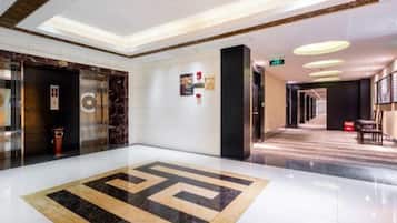 Um hall amplo com um grande design geométrico no chão, um balcão de recepção e um elevador moderno.