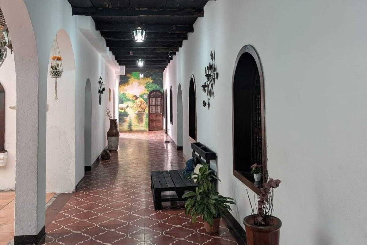 Um corredor com ladrilhos estampados no chão, paredes brancas e vigas de madeira no teto.
