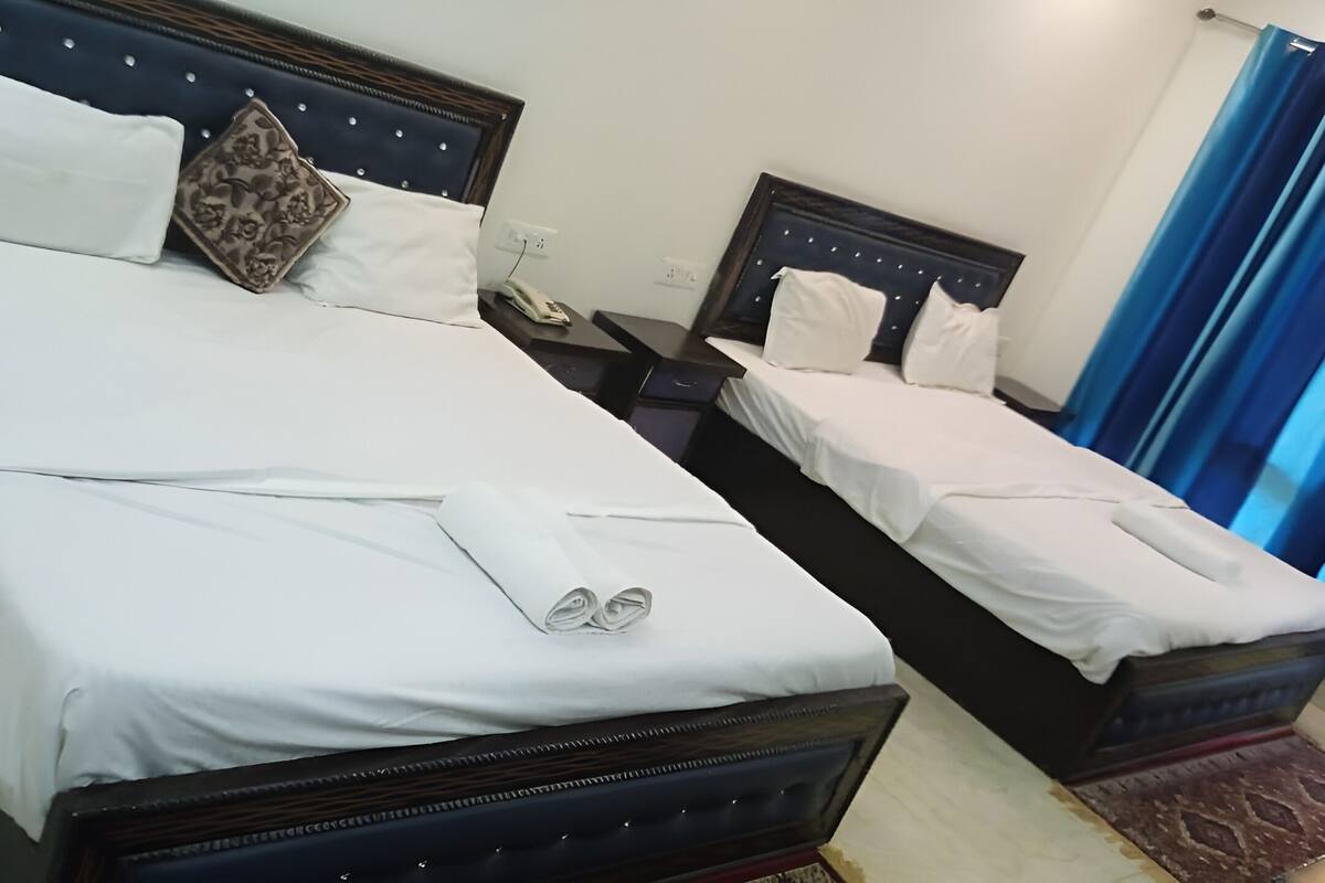 Quarto de hotel com duas camas, cada uma com roupa de cama e almofadas brancas, cabeceira de madeira e mesa de cabeceira com telefone.