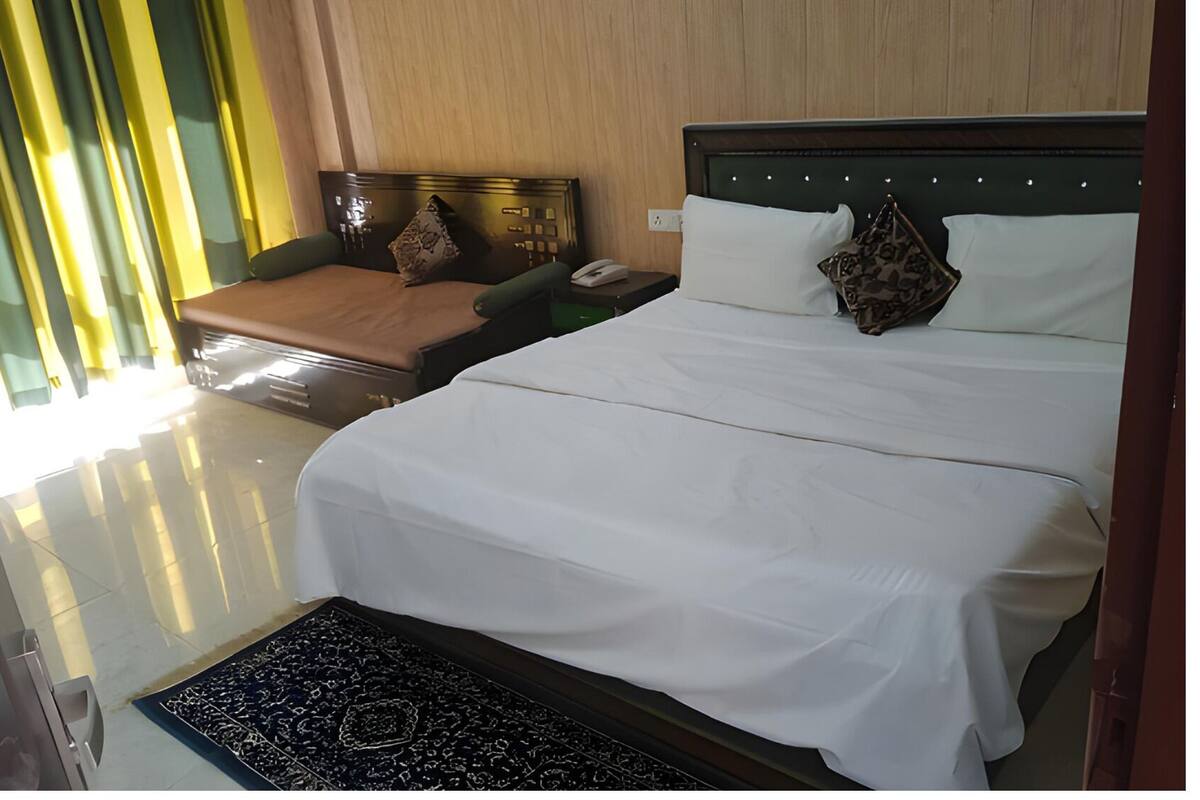 Quarto de hotel com uma cama grande, mesa de cabeceira, cadeira e uma pequena mesa com um telefone.