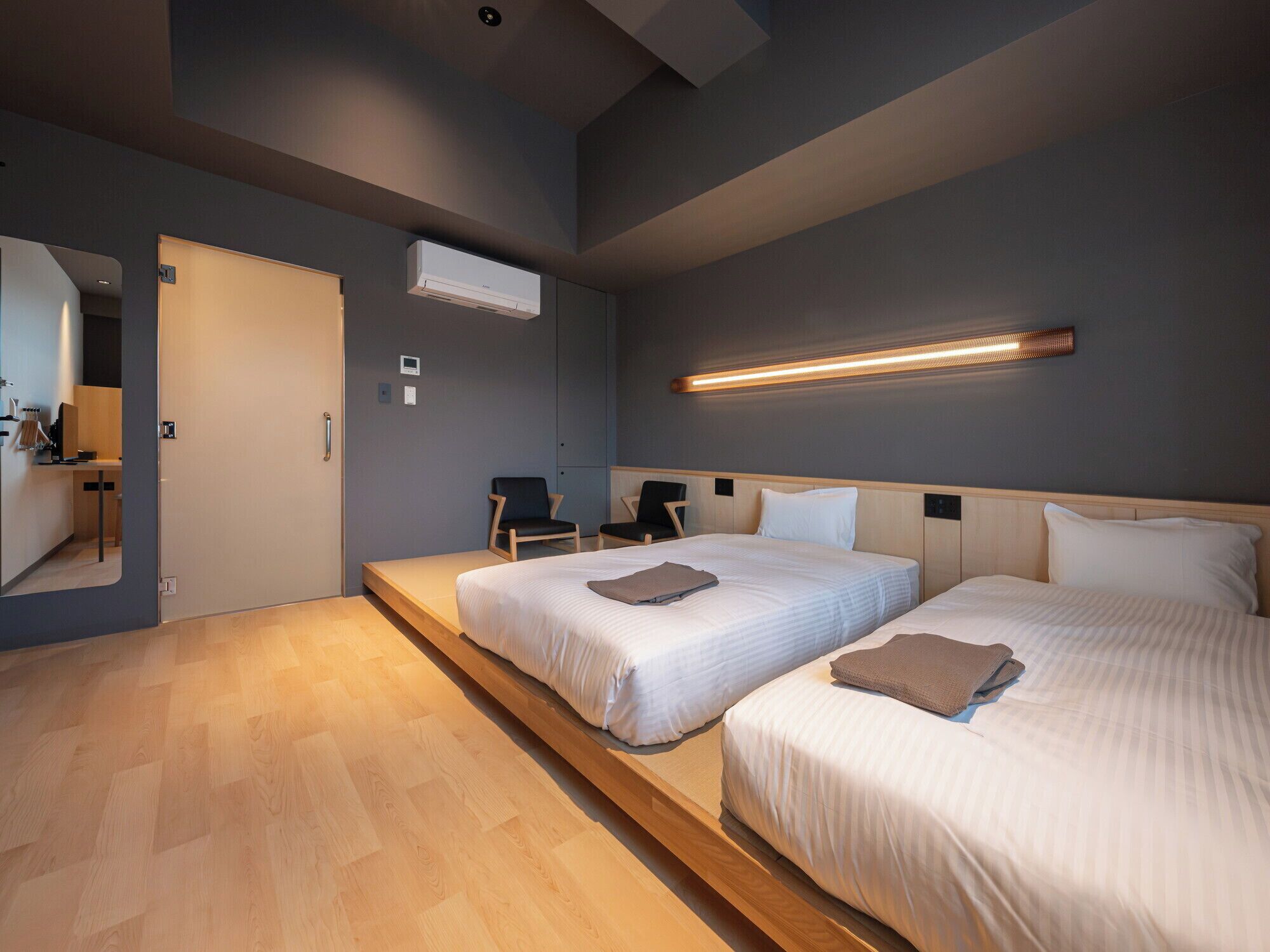 Quarto de hotel moderno com duas camas, uma escrivaninha e uma cadeira.