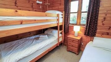 Quarto de cabana de madeira com beliches, mesa de cabeceira com abajur e janela com cortinas.