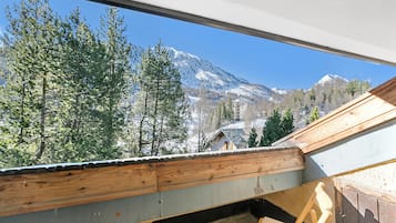 Quarto com vista para montanhas cobertas de neve, teto de madeira e janela com vista para a paisagem.