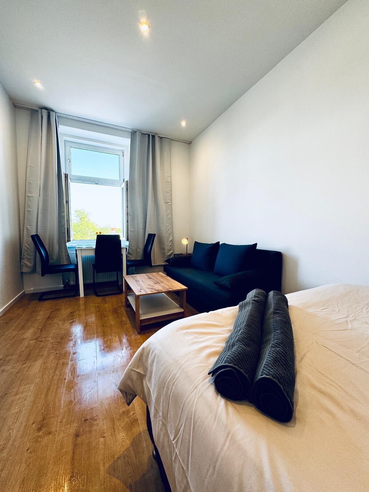 Quarto de hotel com cama, escrivaninha com duas cadeiras, janela com cortinas e vista para o verde lá fora.