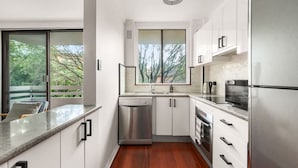 Cozinha moderna com armários brancos, eletrodomésticos de aço inoxidável e uma janela grande com vista para árvores.