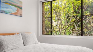 Quarto com cama, janela com vista para árvores e um quadro na parede.