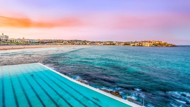 Cena costeira com piscina, praia e edifícios ao fundo.