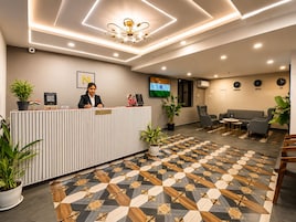 Uma área de recepção com recepcionista, balcão de atendimento, tela digital e um espaço de espera com sofá e poltronas.