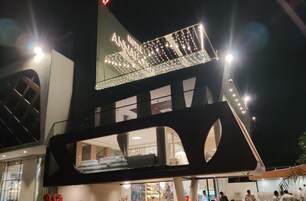 Hotel com design moderno, apresentando uma placa com letras iluminadas, fachada de vidro e amplo interior com áreas de estar visíveis.