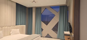 Quarto moderno com uma cama grande, uma televisão e vista do céu noturno por uma janela geométrica.
