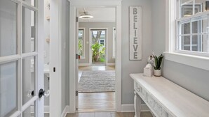 Um corredor com um console branco, um tapete e um letreiro com a palavra 'BELIEVE'.