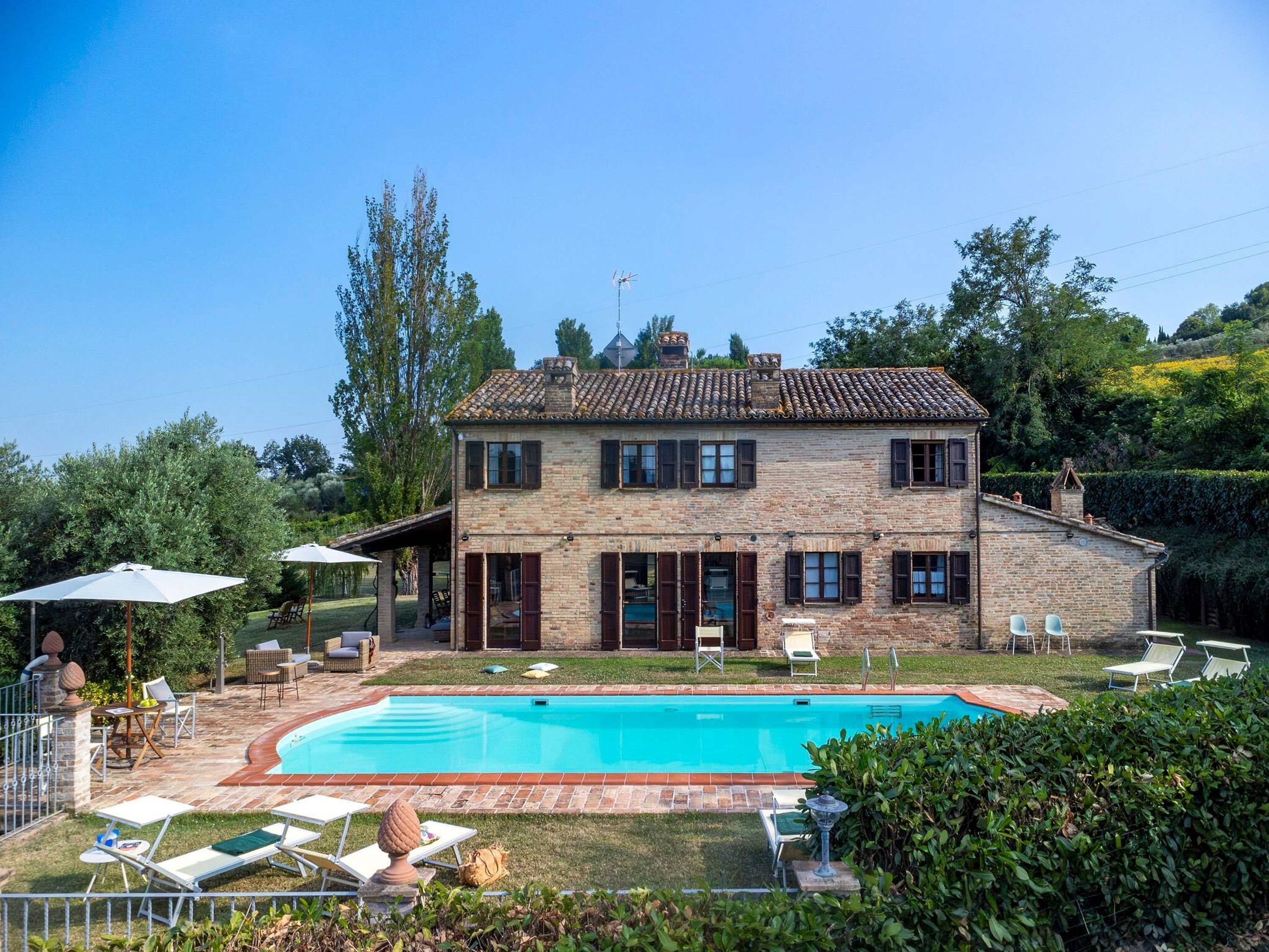 Uma casa de pedra de dois andares com piscina, área de estar ao ar livre e um jardim bem cuidado.