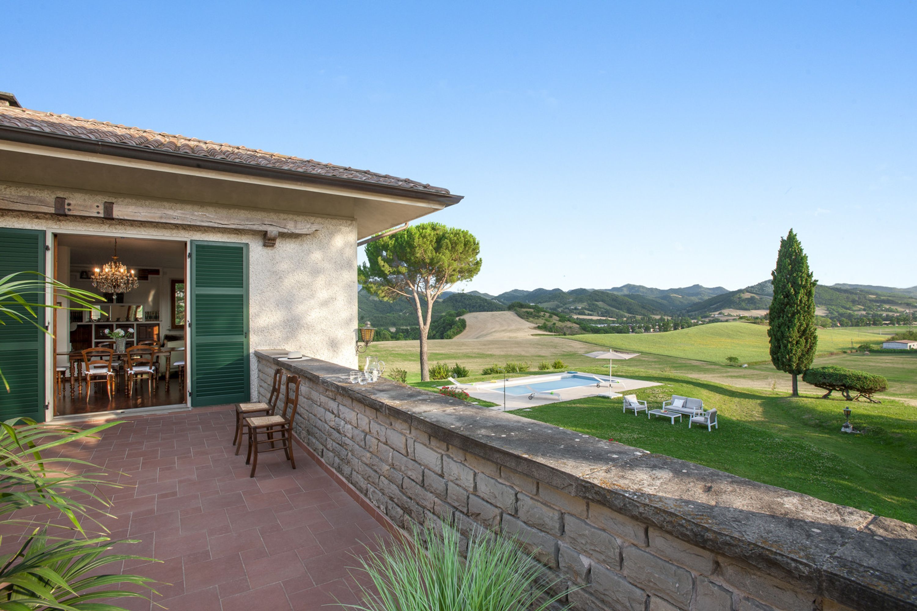 Um pátio com área de refeições, piscina e vista para colinas ondulantes.