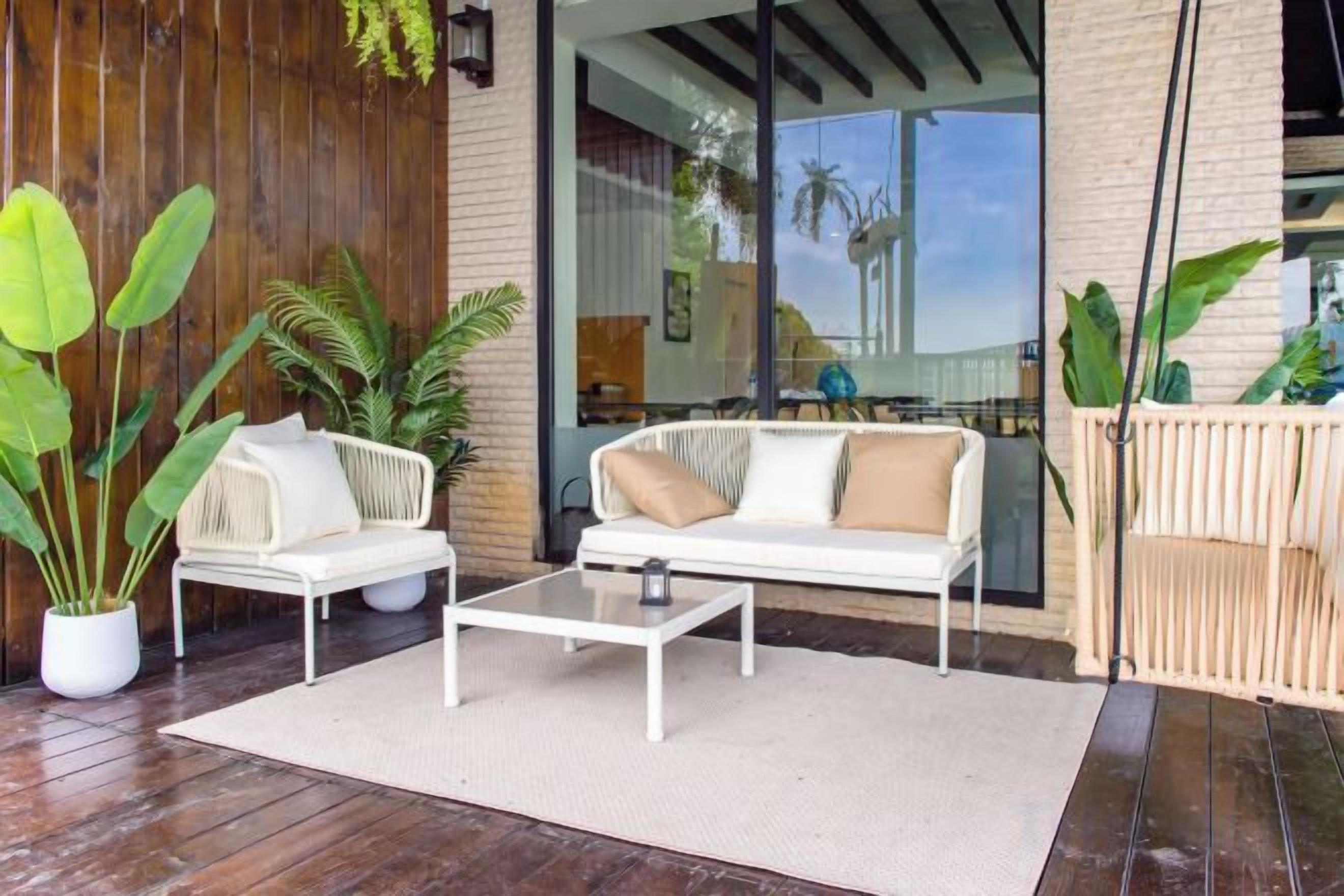 Espaço ao ar livre com assentos, incluindo um sofá e cadeiras brancos, uma mesa de centro e plantas em vasos.