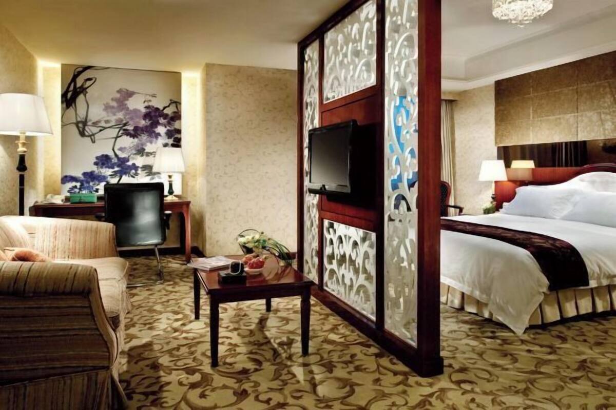 Quarto de hotel com cama, televisão na parede, secretária com cadeira e um biombo decorativo.