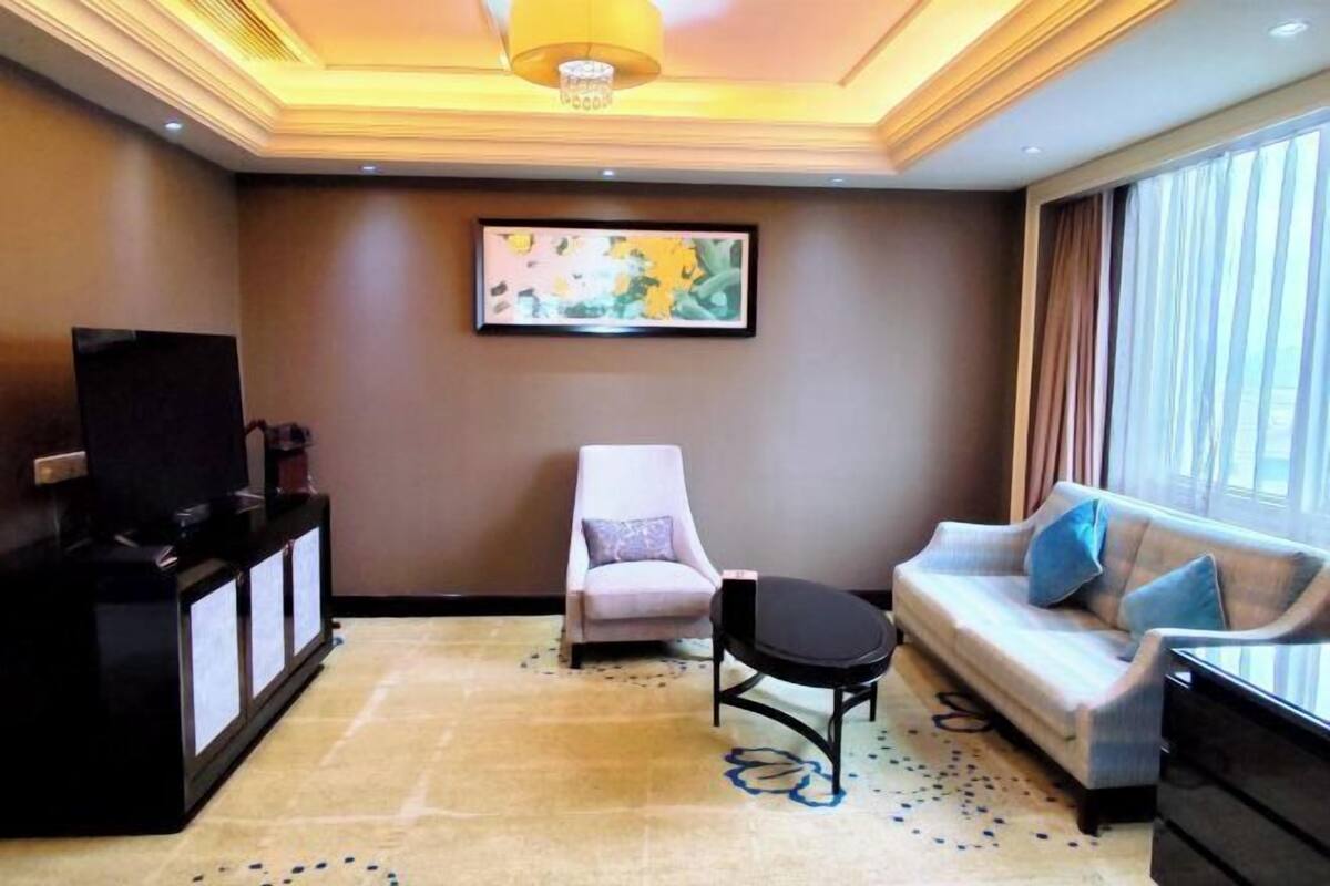 Quarto de hotel com sofá, poltrona, televisão e um quadro na parede.