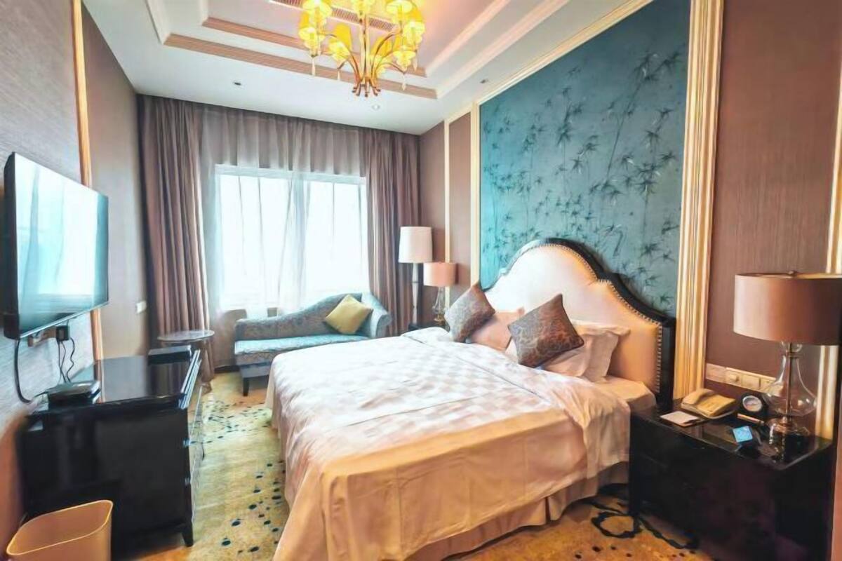 Quarto de hotel com uma cama grande, televisão, escrivaninha e sofá.