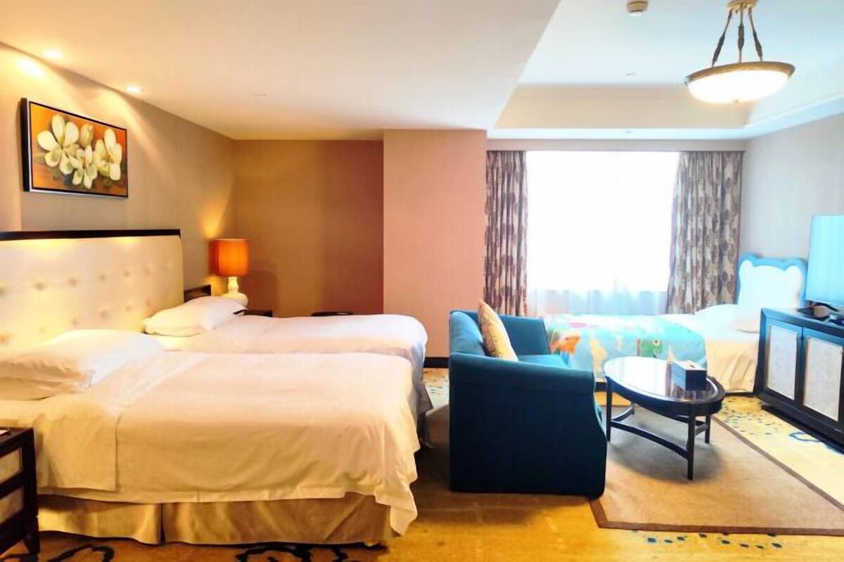 Quarto de hotel com duas camas, um sofá, uma mesinha e um abajur.