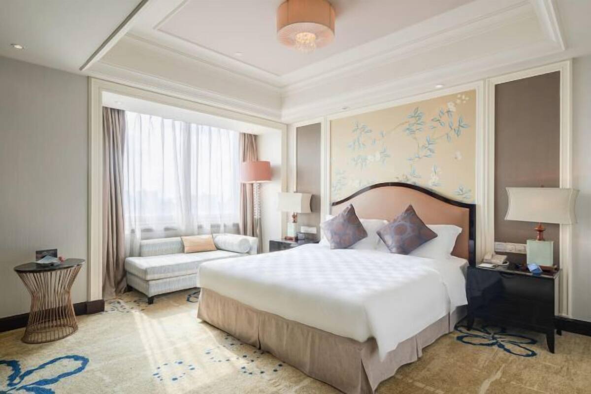 Quarto de hotel com uma cama grande, um sofá, uma mesinha de apoio, uma luminária e um quadro na parede.