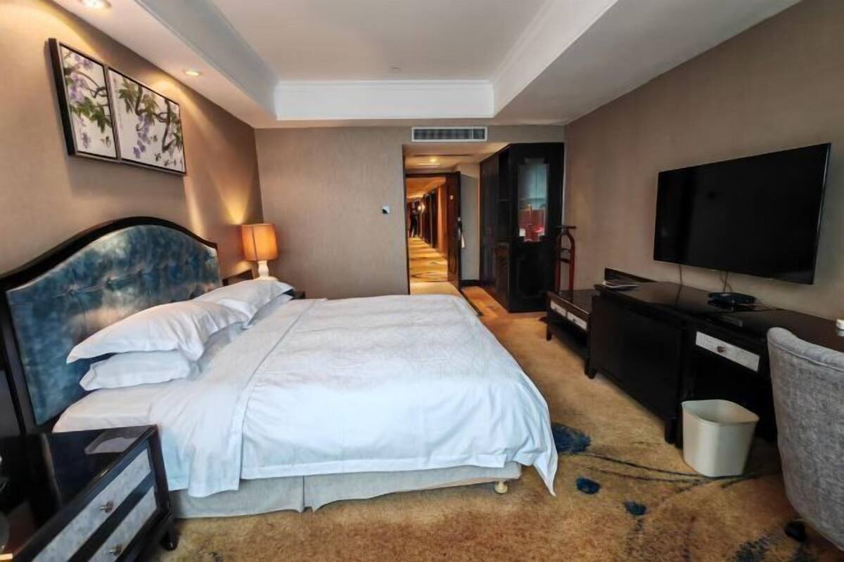 Quarto de hotel com cama, escrivaninha, televisão e obras de arte na parede.